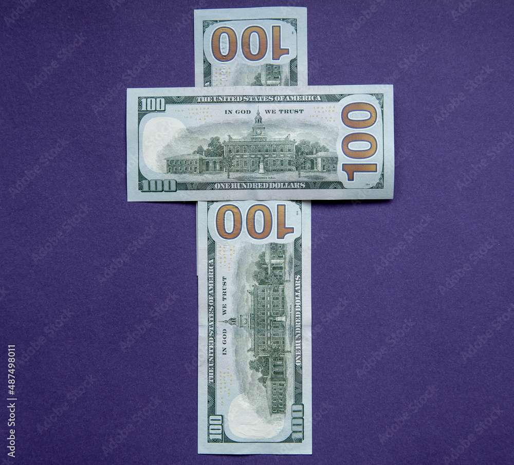 cross folded from one hundred dollar bills on a purple background ...