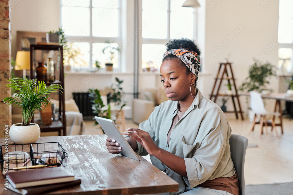Serious young black woman in headscarf sitting at wooden desk and ...