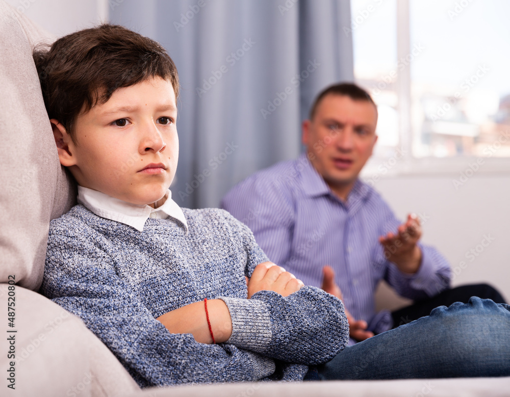 Portrait of troubled preteen boy scolded by his father in home interior ...