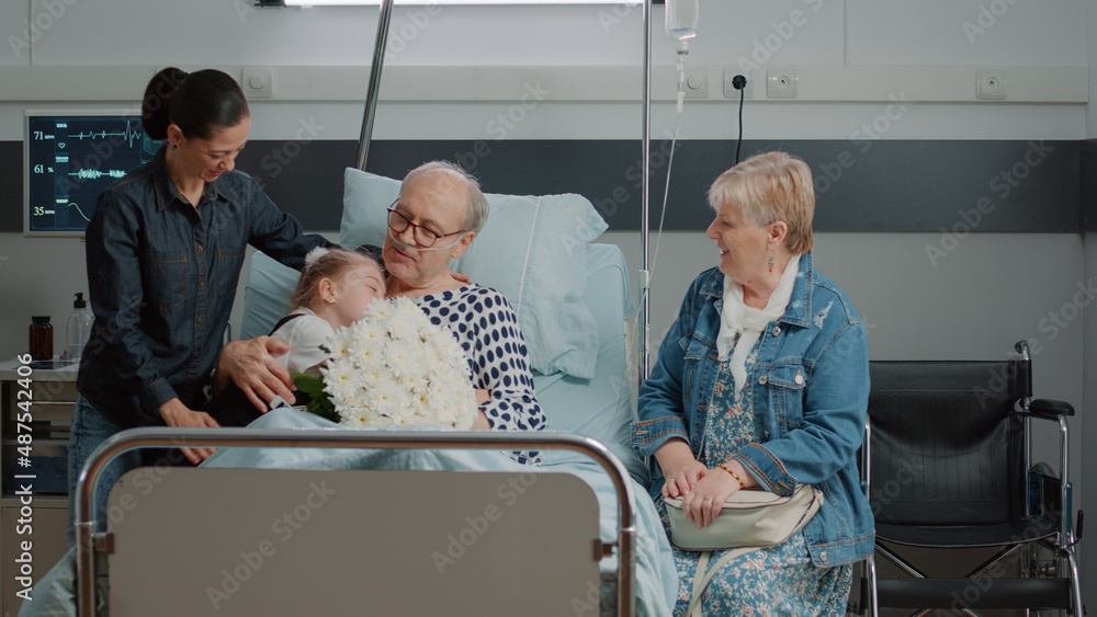 Family visiting old patient and bringing flowers in hospital ward bed ...