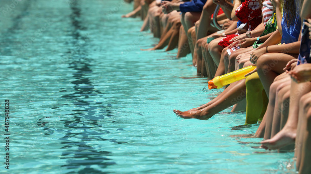 A bright aqua blue swimming pool with students sitting dangling their ...