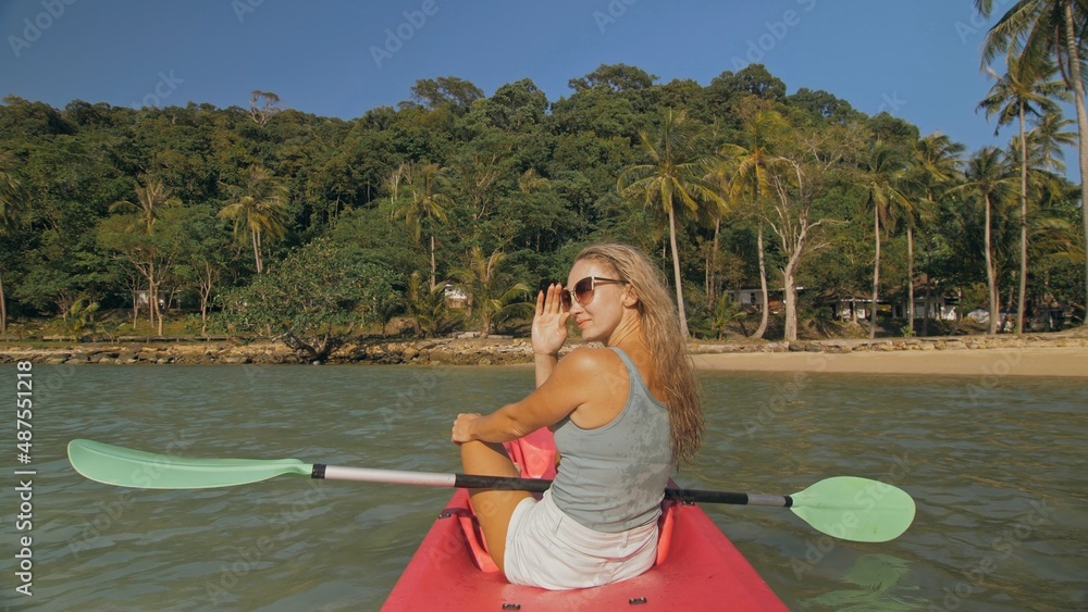 Long haired blonde woman with sunglasses rows bright pink canoe along ...