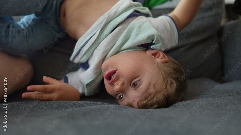 Bored little boy at home in upside down on sofa child playing alone ...