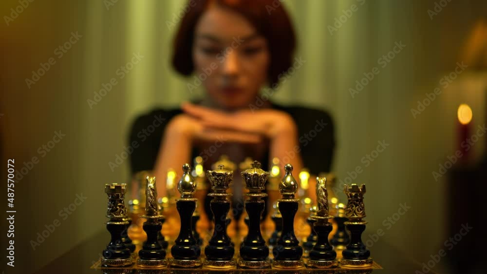 Blurred redhead female chess player moving piece thinking sitting ...