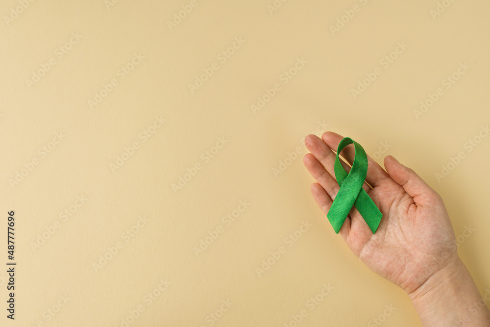 World bipolar day. Adult hand holding green ribbon on beige background ...