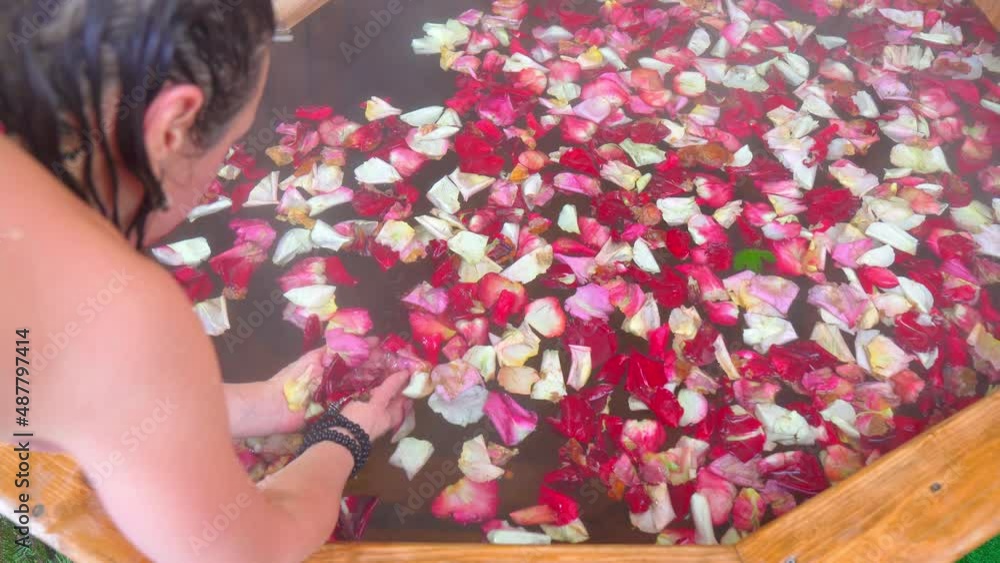 Beautiful young woman lying in a hot ofuro bath full of rose flowers ...