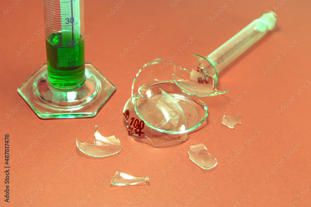 Broken laboratory glass. Green liquid in measuring glass. Failed lab ...