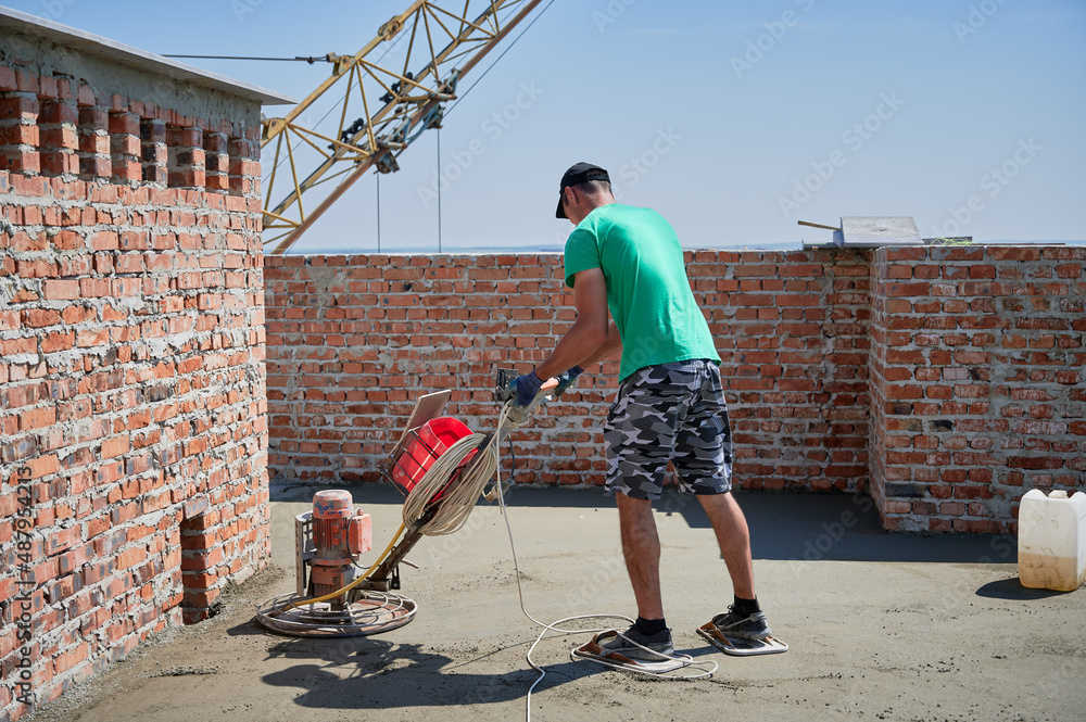 Full length of man builder using troweling machine while screeding ...