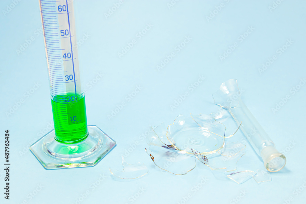 Broken laboratory glass and green liquid in measuring glass on light ...