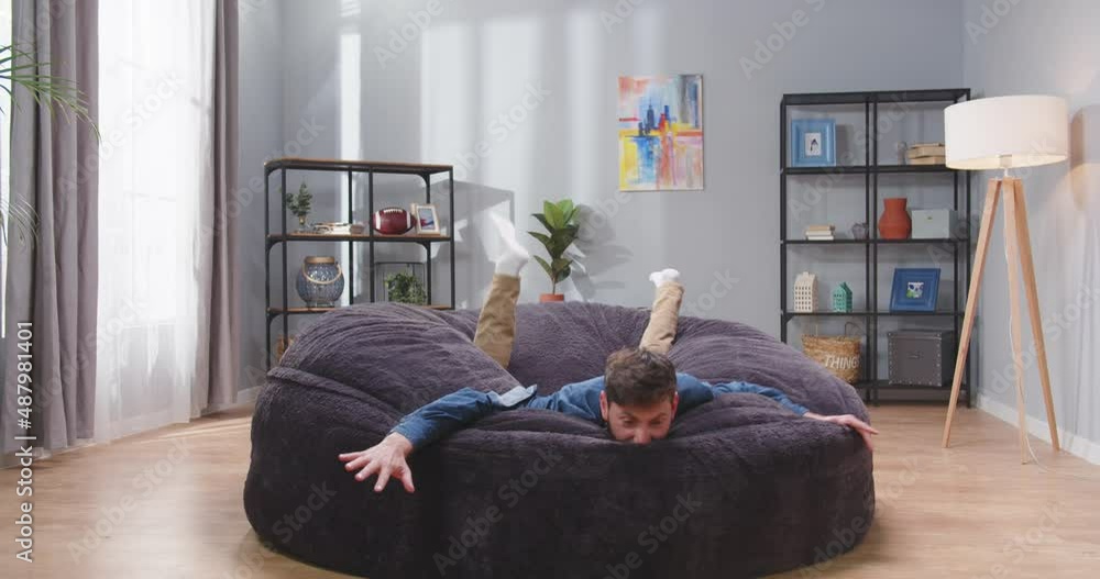 Full height shot of adult man in jeans shirt and beard jumps on sofa in ...