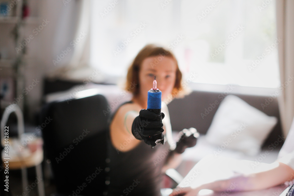 Tattoo parlor, pretty European red-haired girl makes a tattoo on arm ...