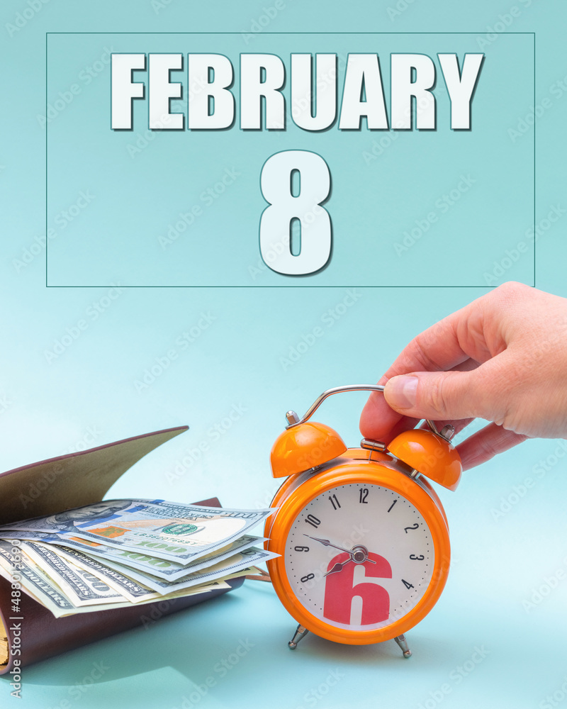 February 8th. Hand holding an orange alarm clock, a wallet with cash ...