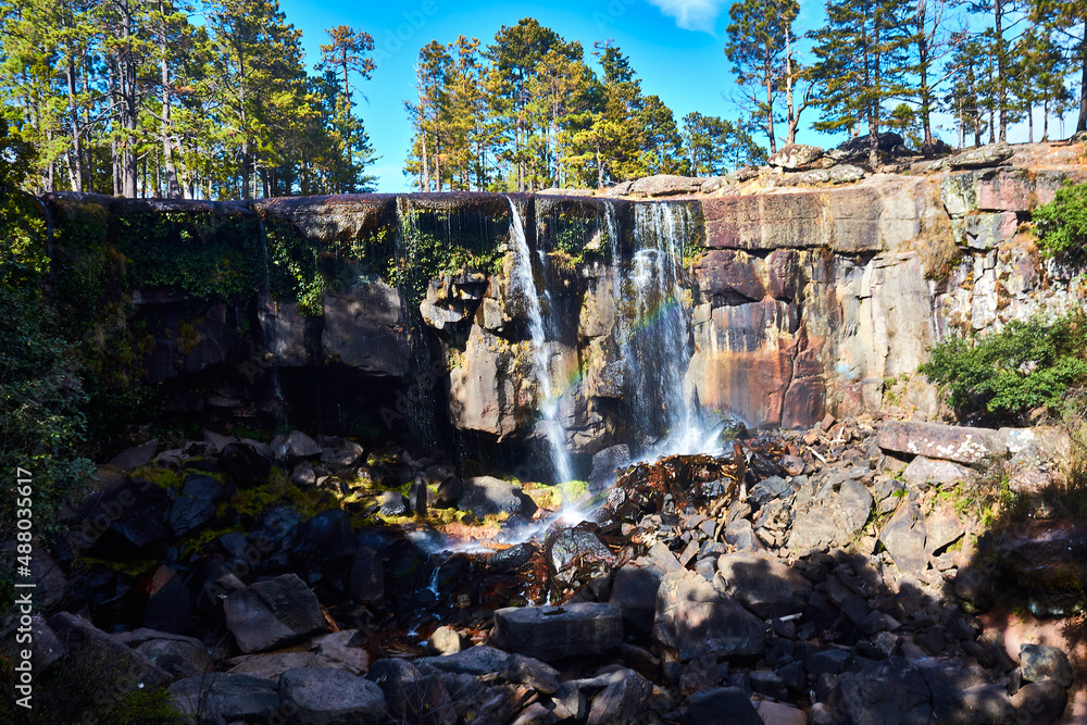 cascada con un arcoiris, rocas en el fondo y pinos al rededor con un ...