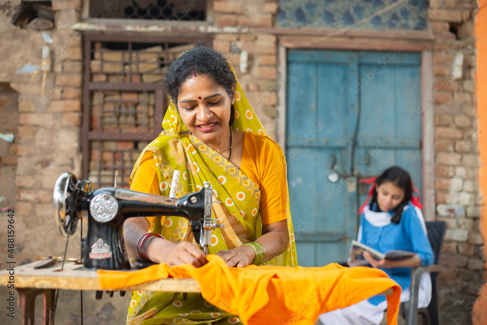 Rural indian woman using sewing machine while her young daughter ...