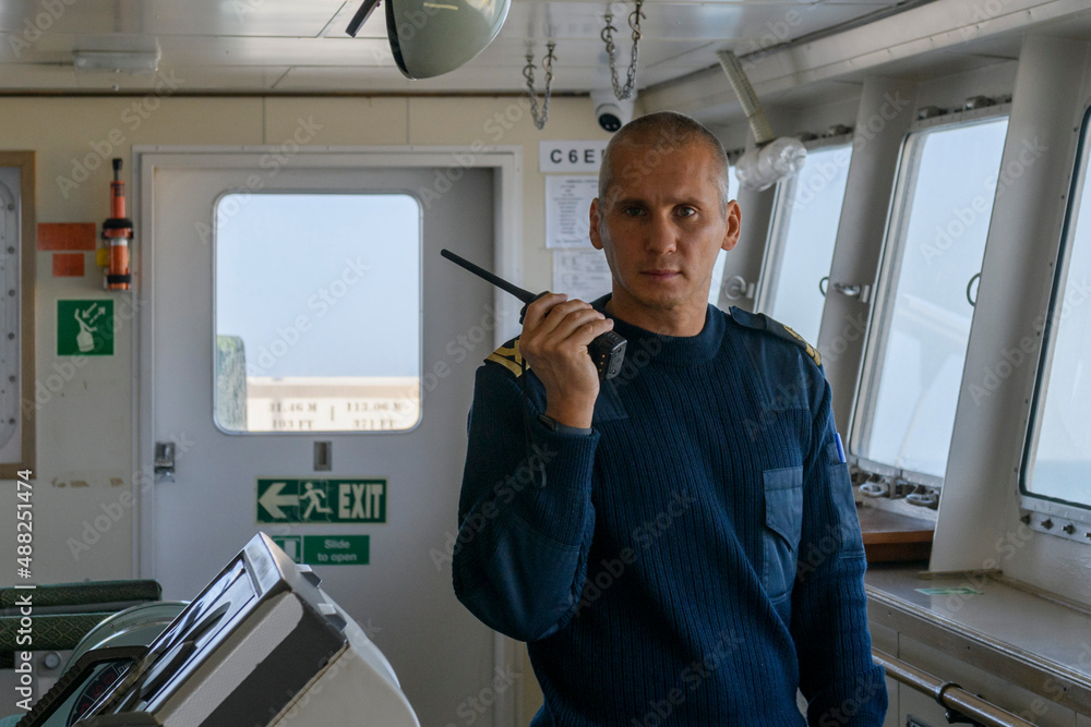 Deck officer on navigational bridge with portable VHF radio. Walkie ...