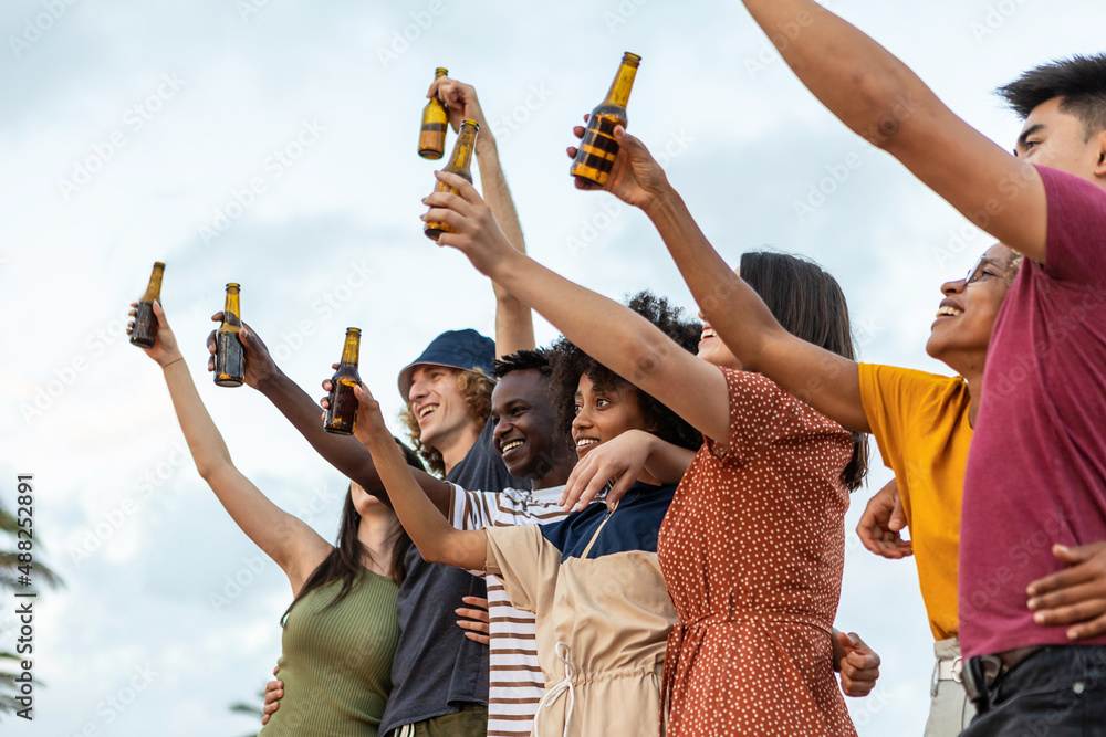 Young group of multiracial friends raising arms while drinking beer at ...