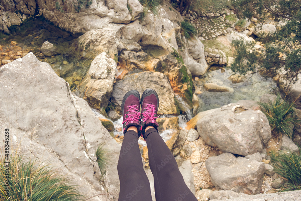 Crop female traveler sitting on rocky cliff with growing grass Stock ...