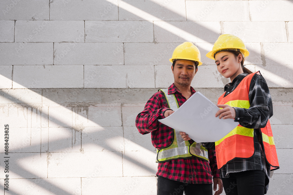 Two Asian civil engineers wear safety hard hats standing hold and look ...