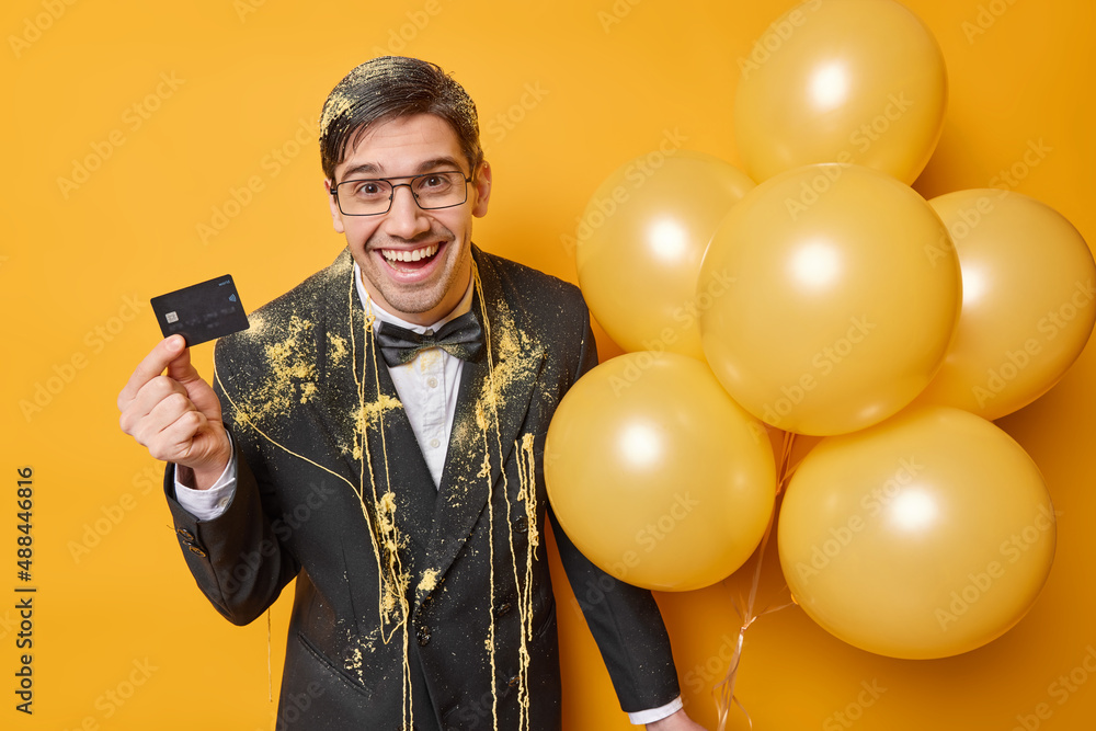 Horizontal shot of handsome positive man holds credit card happy to ...