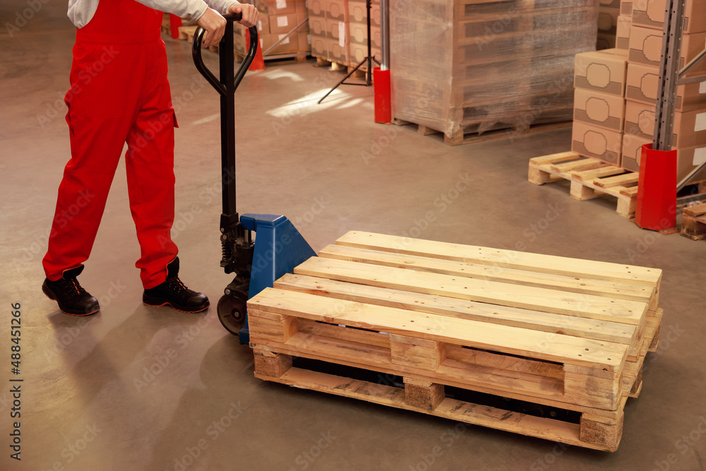Worker moving wooden pallets with manual forklift in warehouse, closeup ...