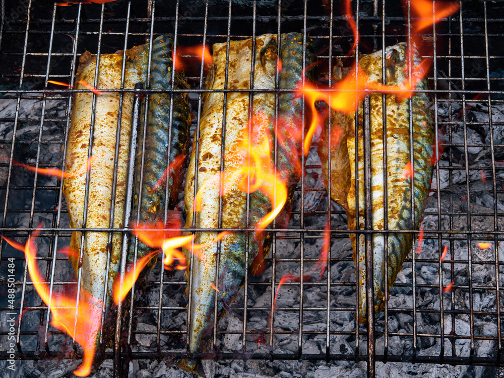 Mackerel fish is baked on a metal grill in a flame of fire. Mackerel ...