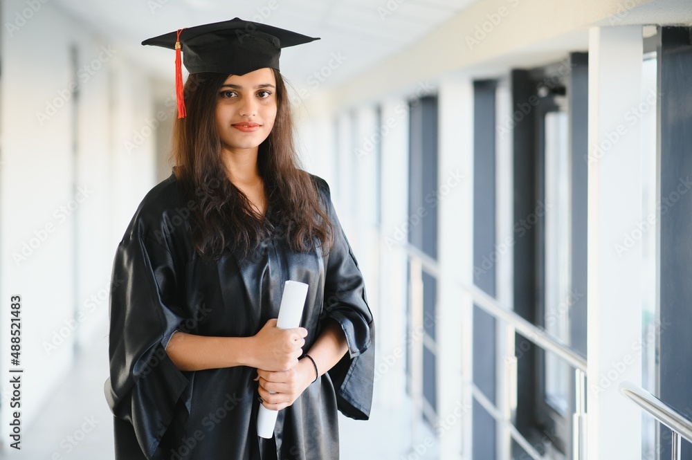 Happy Indian university student in graduation gown and cap holding ...
