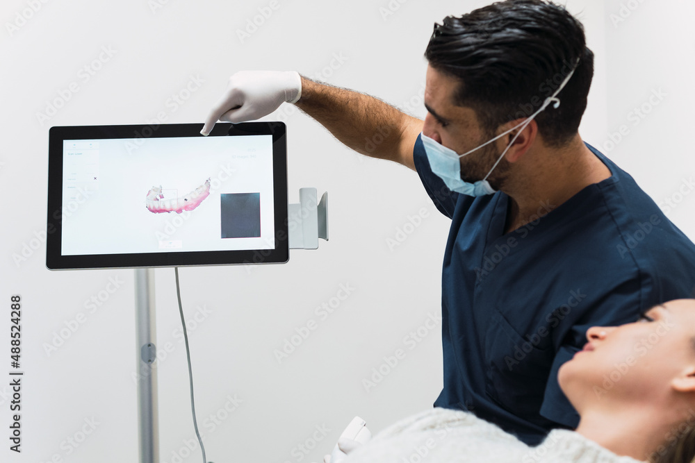Dentist showing teeth X-ray to patient over intraoral scanner screen in ...