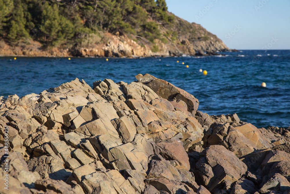 Red brown jagged rocks along the rocky hiking trail Sentier du Littoral ...