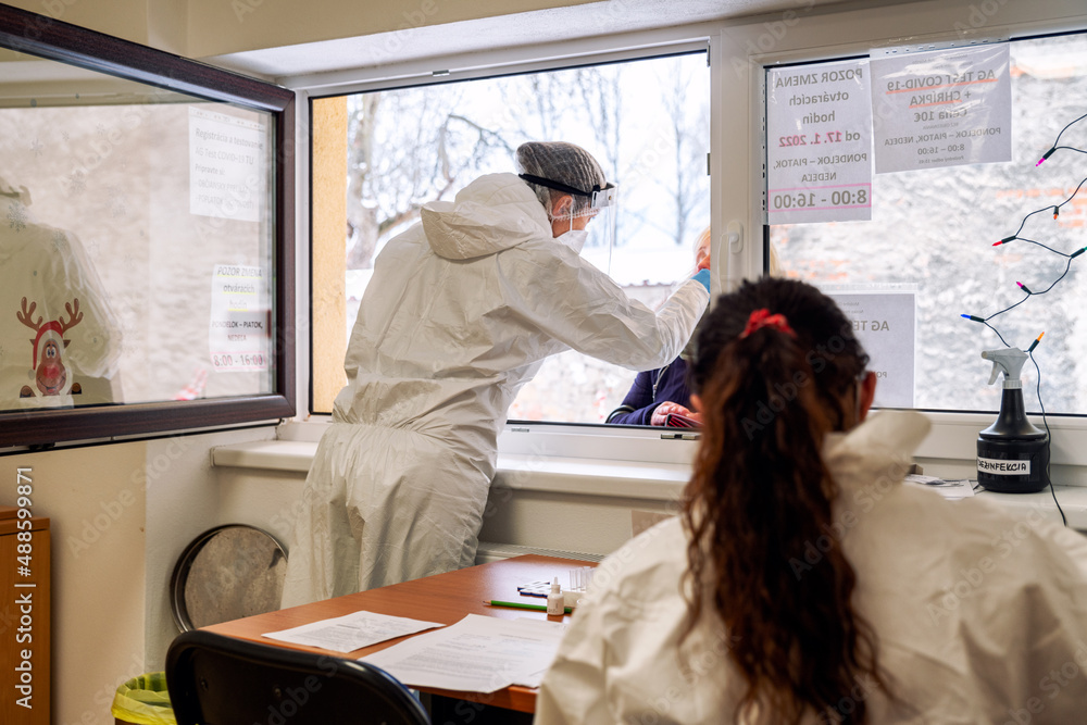 A nurse with shield inserts a swab into a nose to collect a possible ...