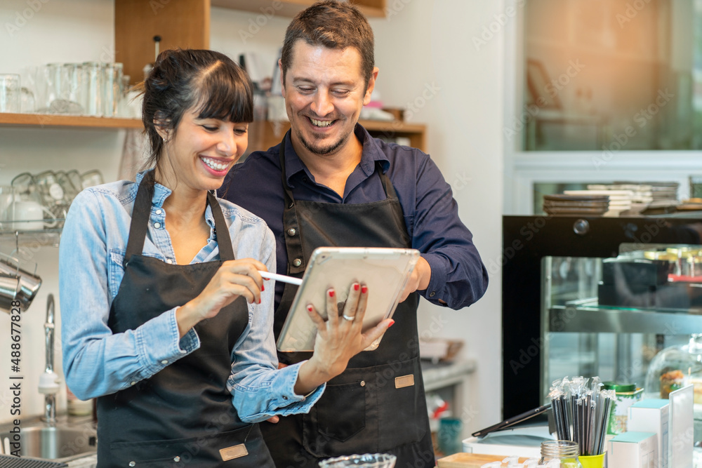 Coffee shop business owner and her husband hold a tablet together to ...