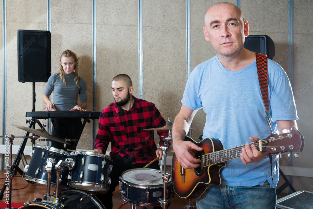 Glad male singer with guitar rehearsing with band of drummer and ...