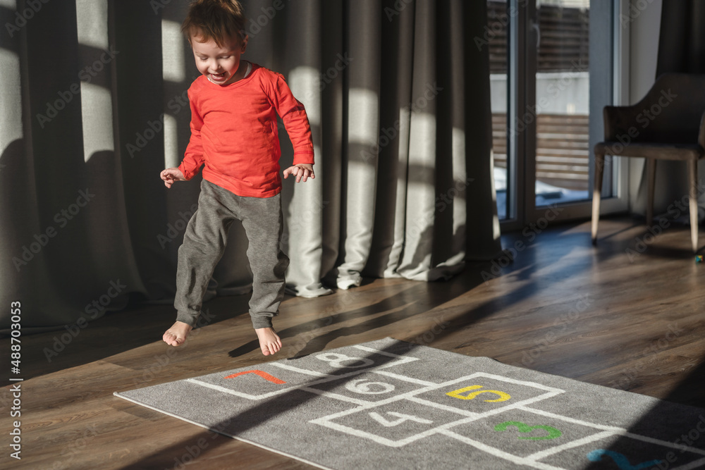 Child, toddler, little boy playing hopscotch, jumping on carpet ...