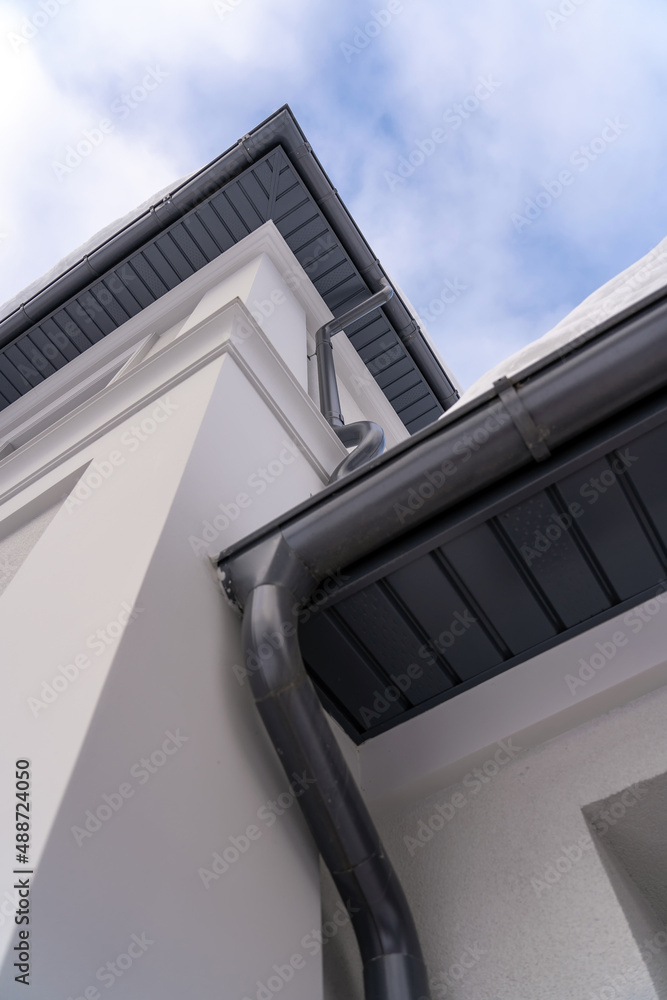 Corner of house with new gray metal tile roof and rain gutter. Metallic ...