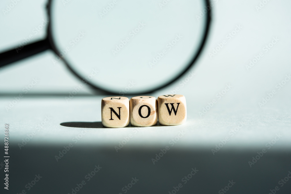 The word now in English, and in the background a magnifying glass ...