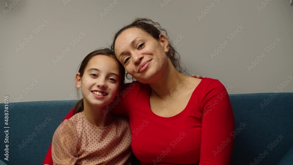 Single mother and daughter sitting on sofa, looking at camera, smiling ...