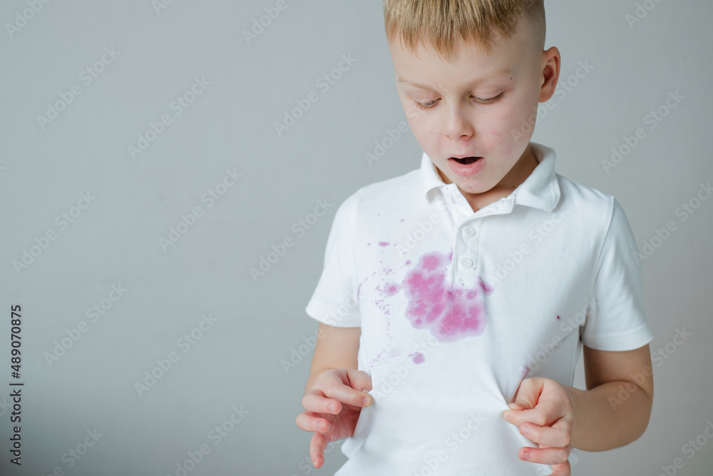 Boy showing a stain spilled juice on his white t-shirt. The concept of ...