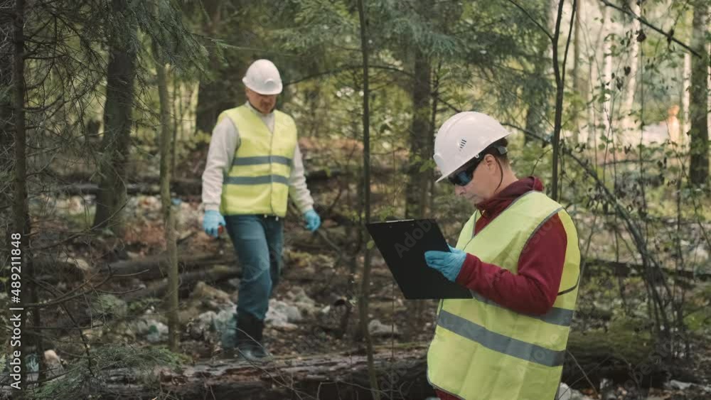 Ecologist man in workwear and helmet collects plastic garbage in forest ...
