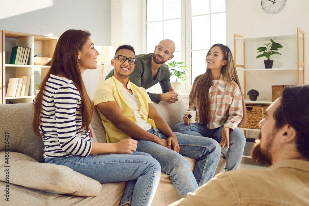 Happy multiethnic friends sit on couch gather at home have fun chatting ...