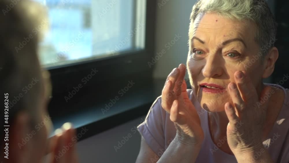 Senior female looking at sagging skin face in mirror, old age ...