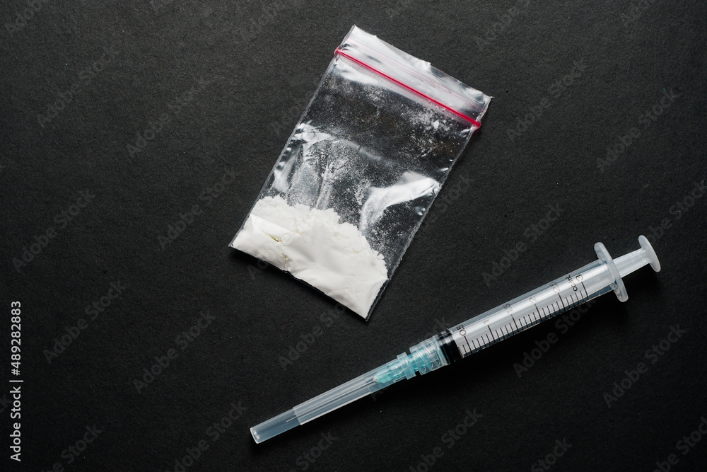 White powder drugs on ziplock plastic bag and syringe on dark table ...