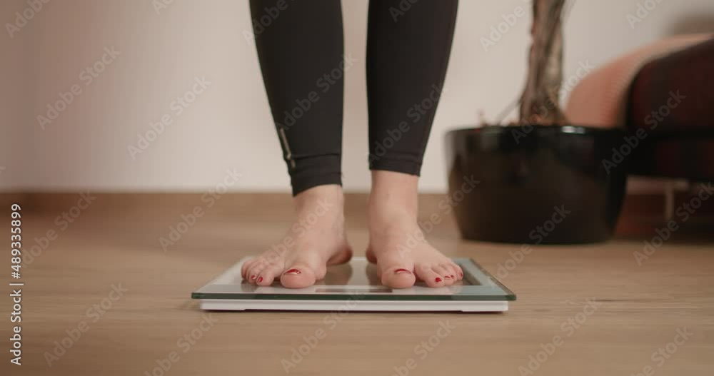 Young woman stepping on scale and wiggling her toes while checking her ...