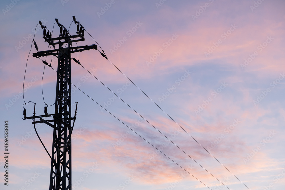 Supports high-voltage powerline pylon against silhouette in epic sunset ...