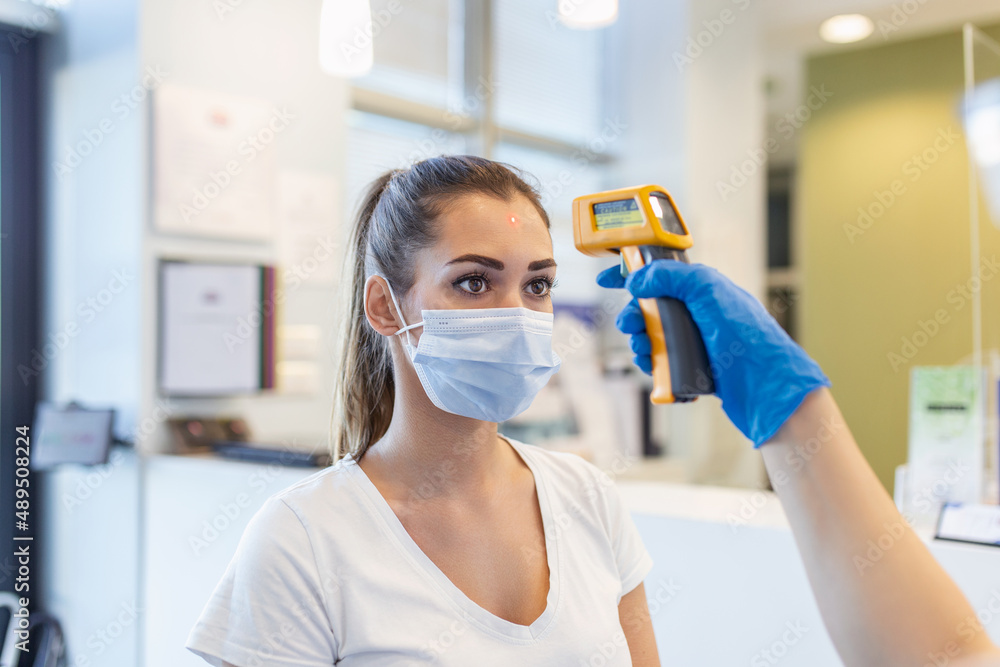 Nurse checking woman's temperature with infrared thermometer at counter ...