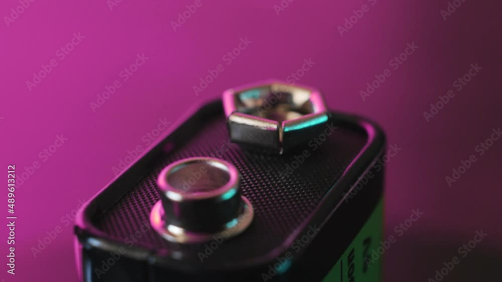 A 9-volt battery rotates and shines in rays of light on a pink ...