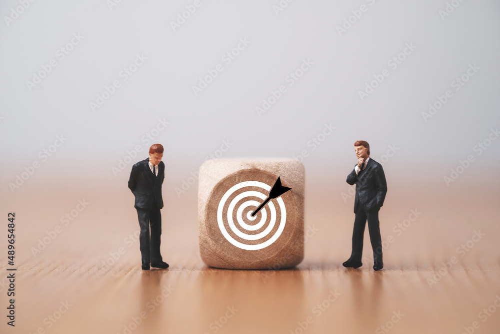 Miniature businessmen figure standing and thinking with cube and target ...