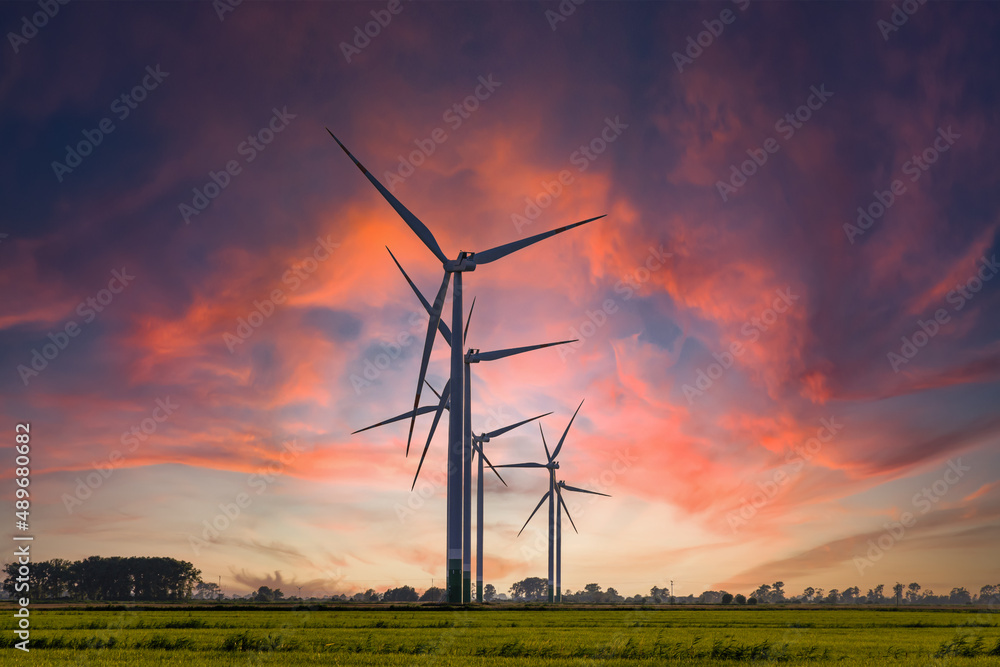 Windmill farm on green meadow under moody red sky, green energy ...