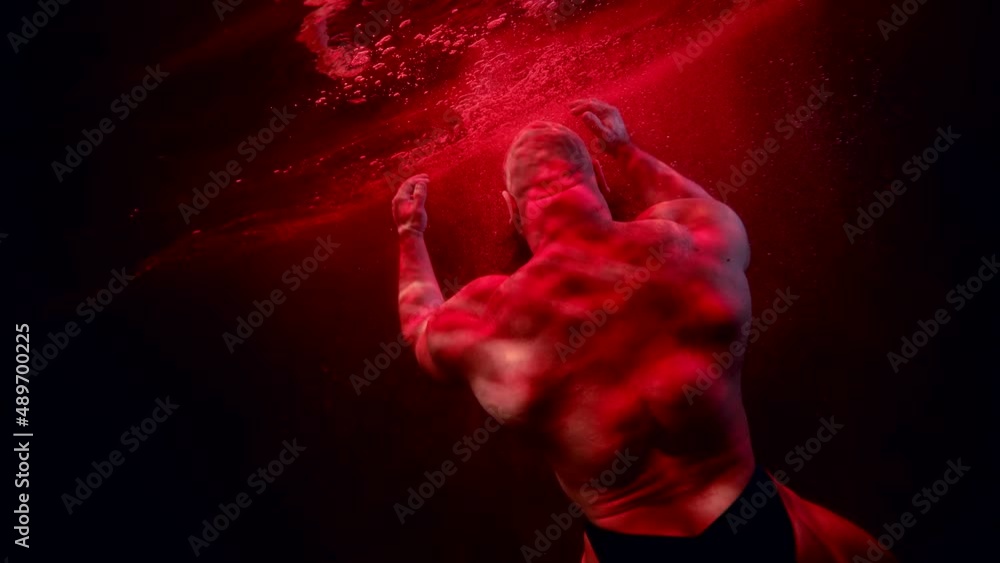 bodybuilder is swimming in red water of pool, rear view on male ...