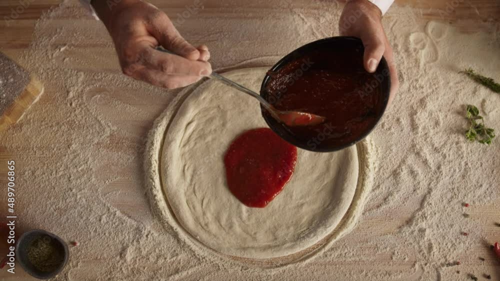 Chef spreading tomato sauce on pizza. Baker man hands cooking food in ...