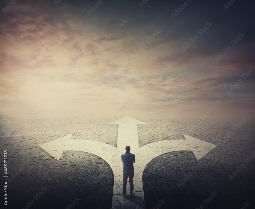 Doubtful businessman stands in front of a crossroad with road split in ...