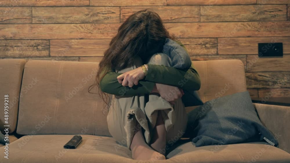 Sad girl sitting on couch hugging her legs with hands. Depression ...